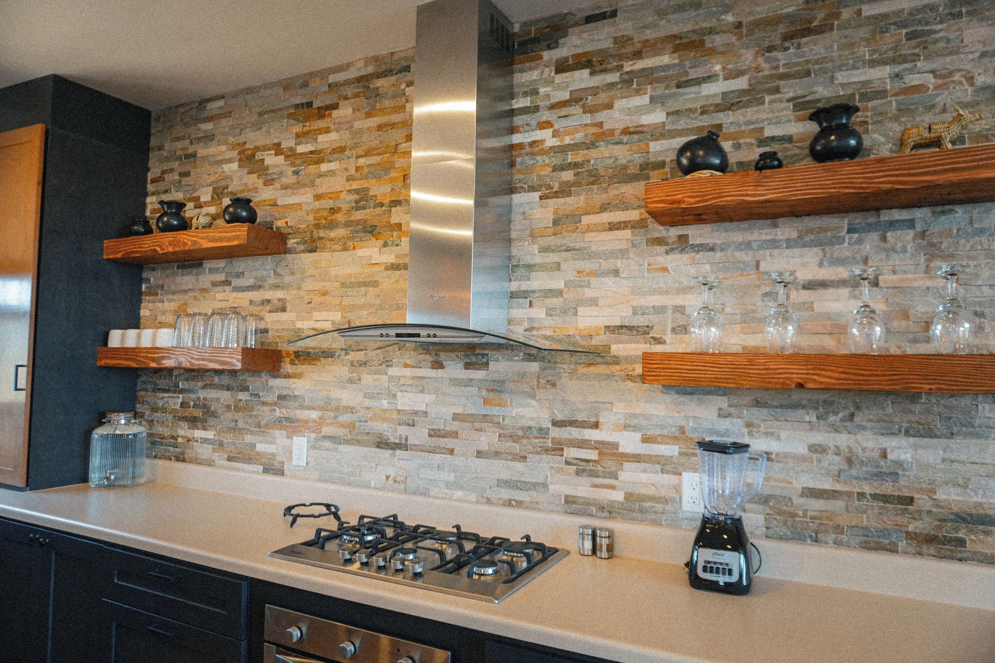 Cozinha com fogão a gás, liquidificador e painel de backsplash de pedra.