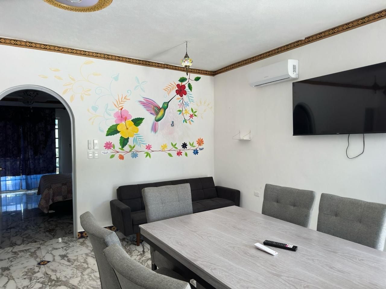 Uma sala de estar moderna com área de jantar, TV fixada na parede e um mural decorativo.