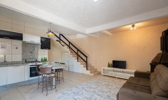 Uma cozinha moderna com área de refeições, uma escada e uma sala de estar com sofá e televisão.