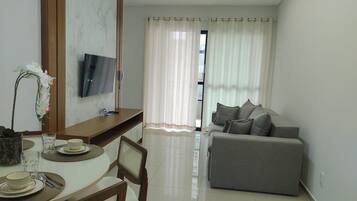 Sala de estar moderna com um sofá cinzento, área de jantar com mesa posta para dois e TV na parede.