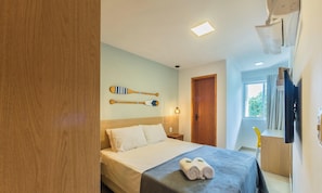 Quarto de hotel com cama, cabeceira de madeira, luminária na parede, porta e janela.