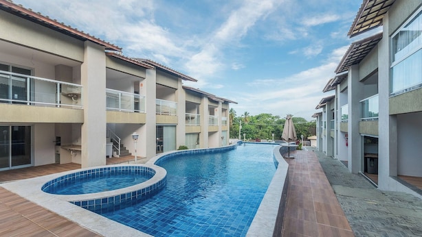 Uma piscina com design curvo, rodeada por edifícios com varandas e grandes janelas.