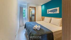 Quarto de hotel com cama, parede de destaque verde-água e uma obra de arte com baleias.