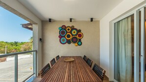 Uma mesa de jantar de madeira com seis cadeiras, uma obra de arte abstrata na parede e uma porta de vidro à direita.