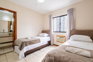 Quarto de hotel com duas camas, banheiro com espelho e pia, e janela com cortinas.