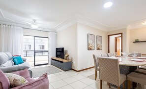 Uma sala de estar com sofá, televisão, mesa de jantar com cadeiras e ventilador de teto.