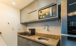 Uma cozinha moderna com micro-ondas embutido, geladeira de aço inoxidável e bancada de granito.