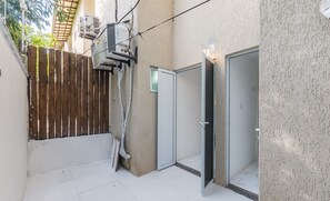 Um corredor externo estreito com cerca de madeira, porta deslizante e unidade de ar condicionado na parede.