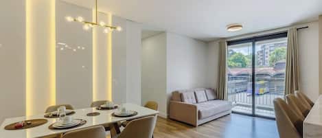 Uma área de refeições moderna com uma mesa posta para quatro pessoas, um sofá e uma varanda com vista para edifícios.