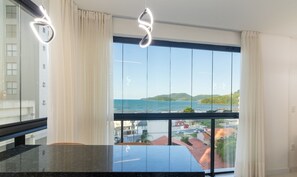 Quarto moderno com uma janela ampla, bancada de mármore e vista para o mar.