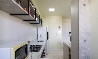 Uma cozinha moderna com micro-ondas, fogão e pia embutidos. Há uma prateleira acima da pia com diversos objetos.
