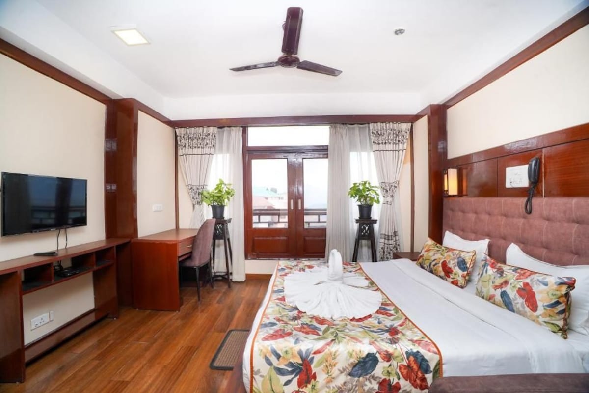Quarto de hotel com cama, televisão, escrivaninha e ventoinha no teto.