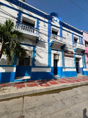 Um edifício com fachada azul e branca, uma varanda e uma placa indicando que é um hotel.