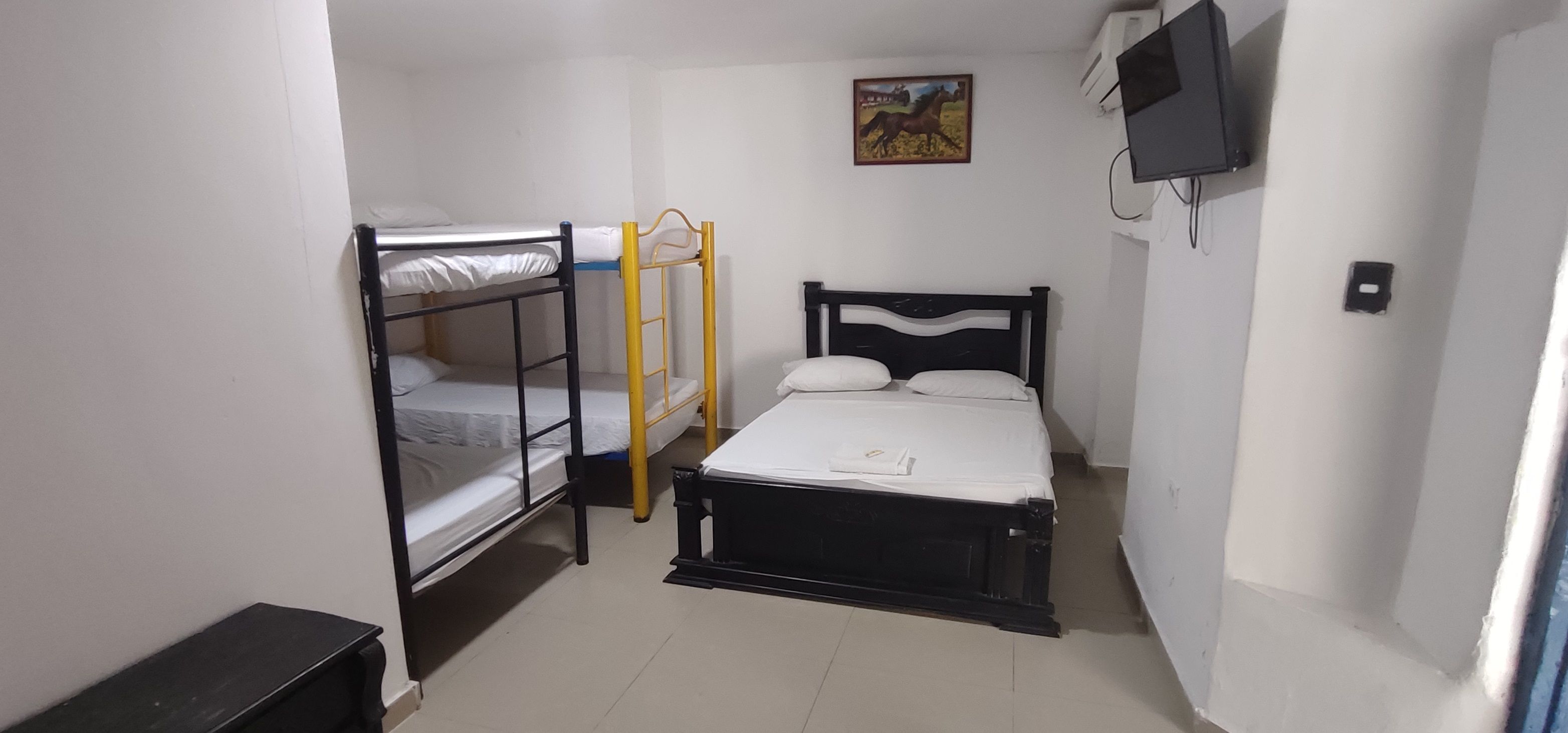 Quarto com beliches, uma cama de solteiro, televisão fixada na parede e um quadro.