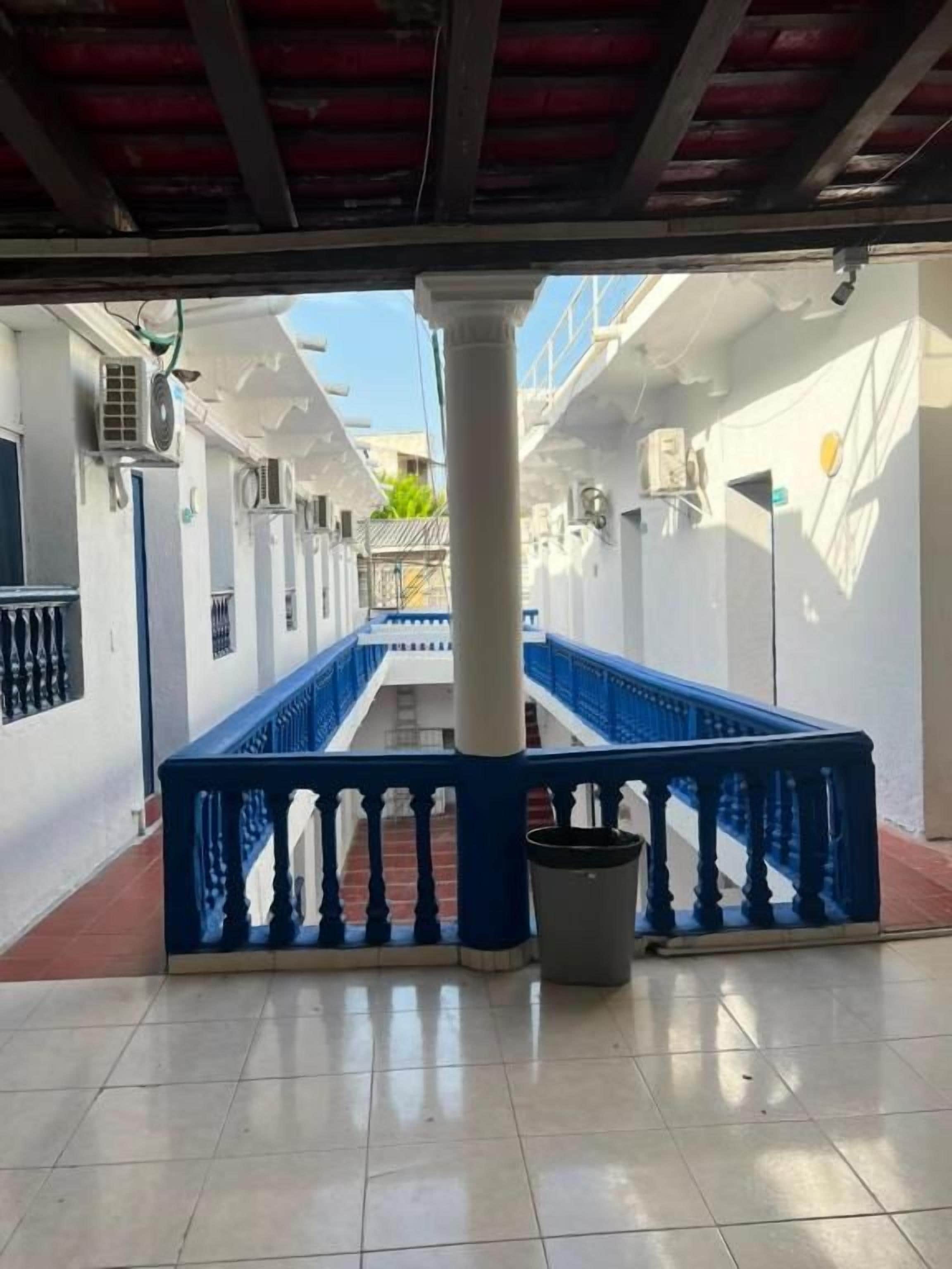 Um corredor com corrimão azul, paredes brancas e chão de azulejos.