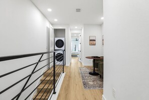 Um corredor moderno com escada, máquina de lavar, ventilador de teto e uma pequena mesa com tapete.