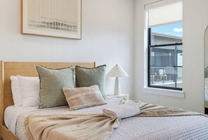 Uma cama bem arrumada com cabeceira, travesseiros e um cobertor. Há uma janela com vista para o exterior.