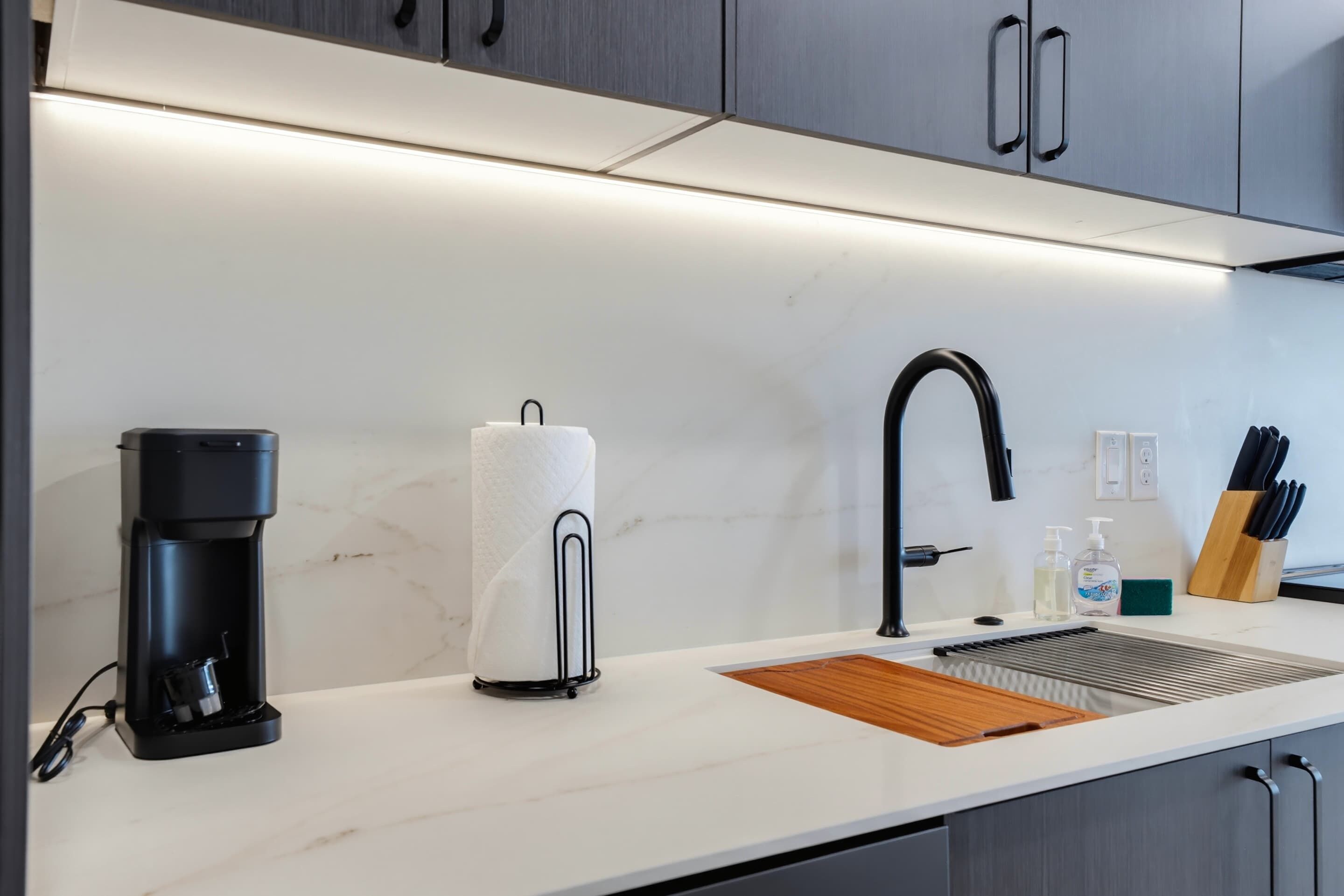 Uma cozinha moderna com cafeteira, porta-toalhas de papel, pia e porta-facas.