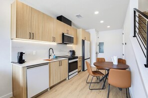 Uma cozinha moderna com armários de madeira, micro-ondas, frigorífico, pia e um espaço de refeições com cadeiras.