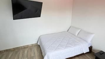 Quarto com cama, TV fixada na parede e piso de madeira.