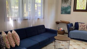 Sala de estar com um sofá azul, uma mesa de centro redonda e um quadro na parede.