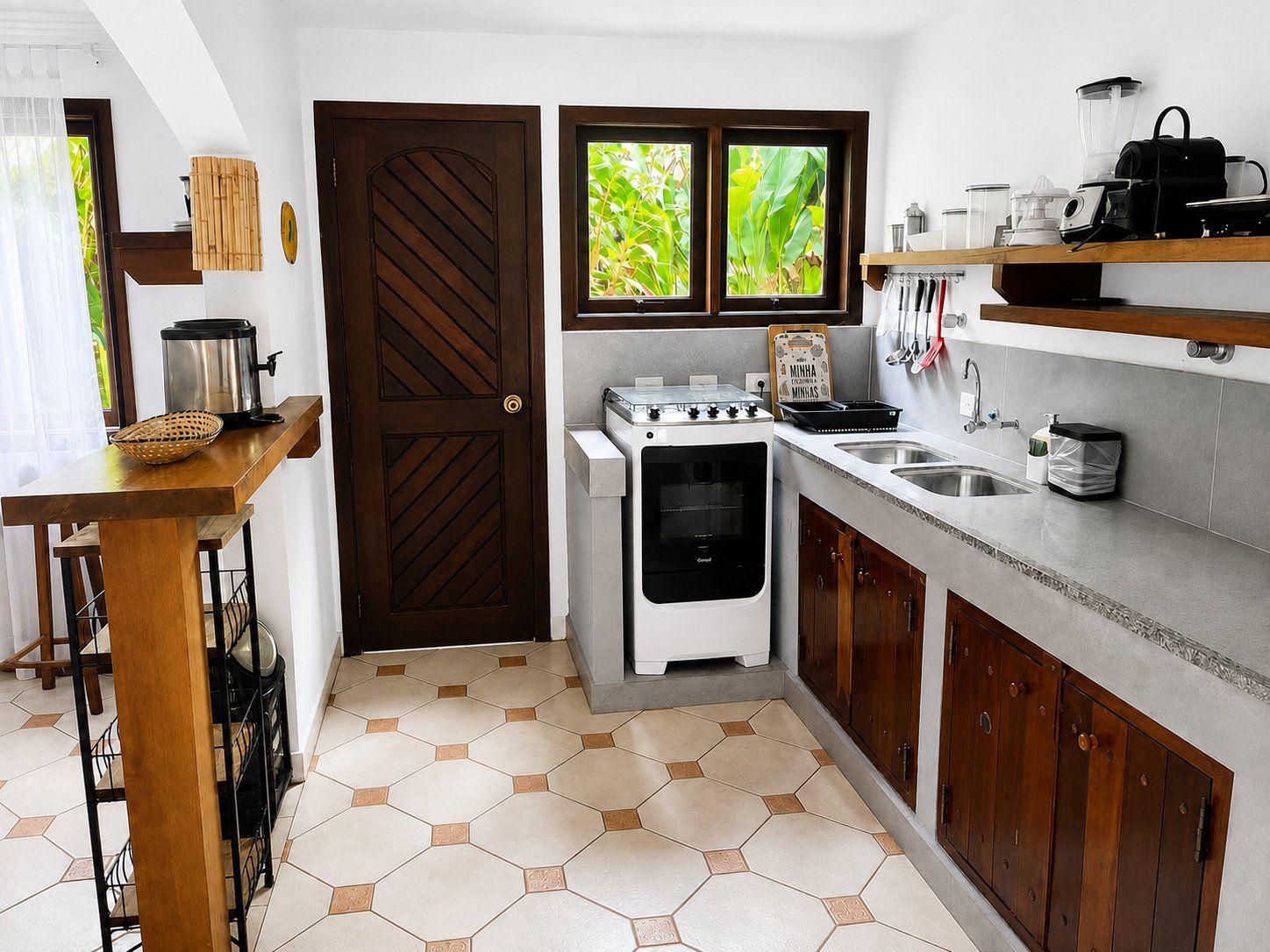 Cozinha compacta com fogão, forno e pia, armários de madeira e janela com vista para o verde.