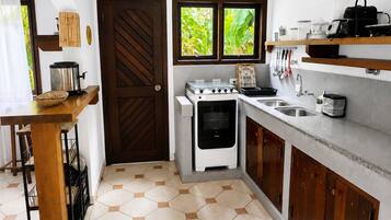 Cozinha compacta com fogão, forno e pia, armários de madeira e janela com vista para o verde.