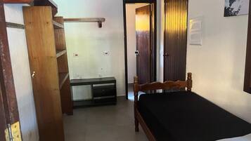Quarto com cama de madeira, mesa de cabeceira, cômoda, guarda-roupa e porta que dá para outro espaço.