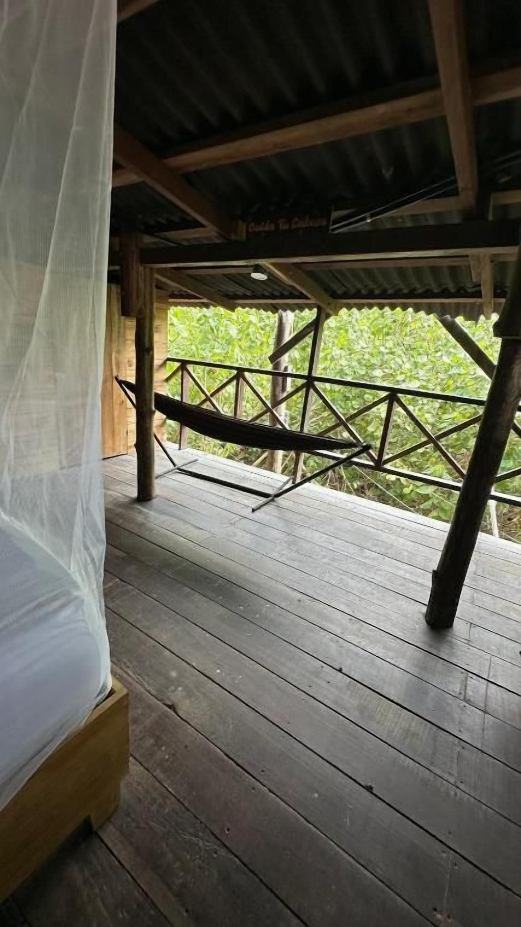 Um deck de madeira com uma rede, uma cama com dossel e vista para o verde.