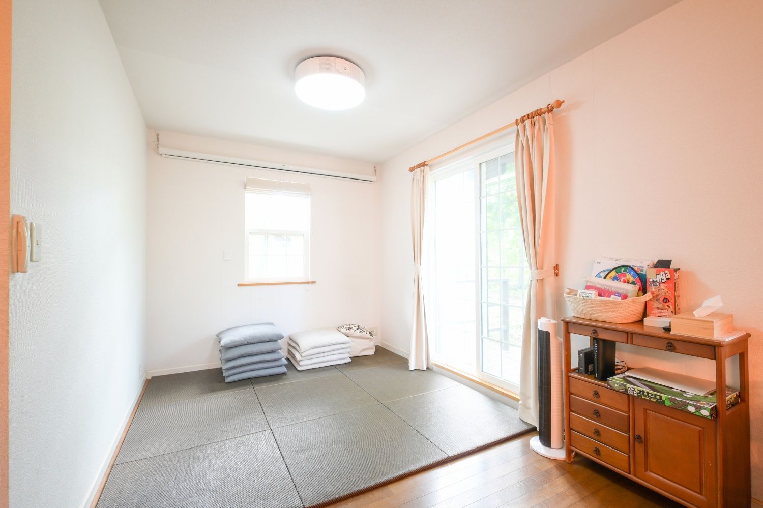 Quarto com uma janela grande, um radiador, uma prateleira com objetos e um tapete no chão.