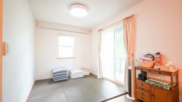 Quarto com uma janela grande, um radiador, uma prateleira com objetos e um tapete no chão.