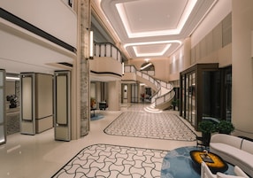 Um hall amplo com escadaria central, piso estampado e área de estar com mesa de centro.
