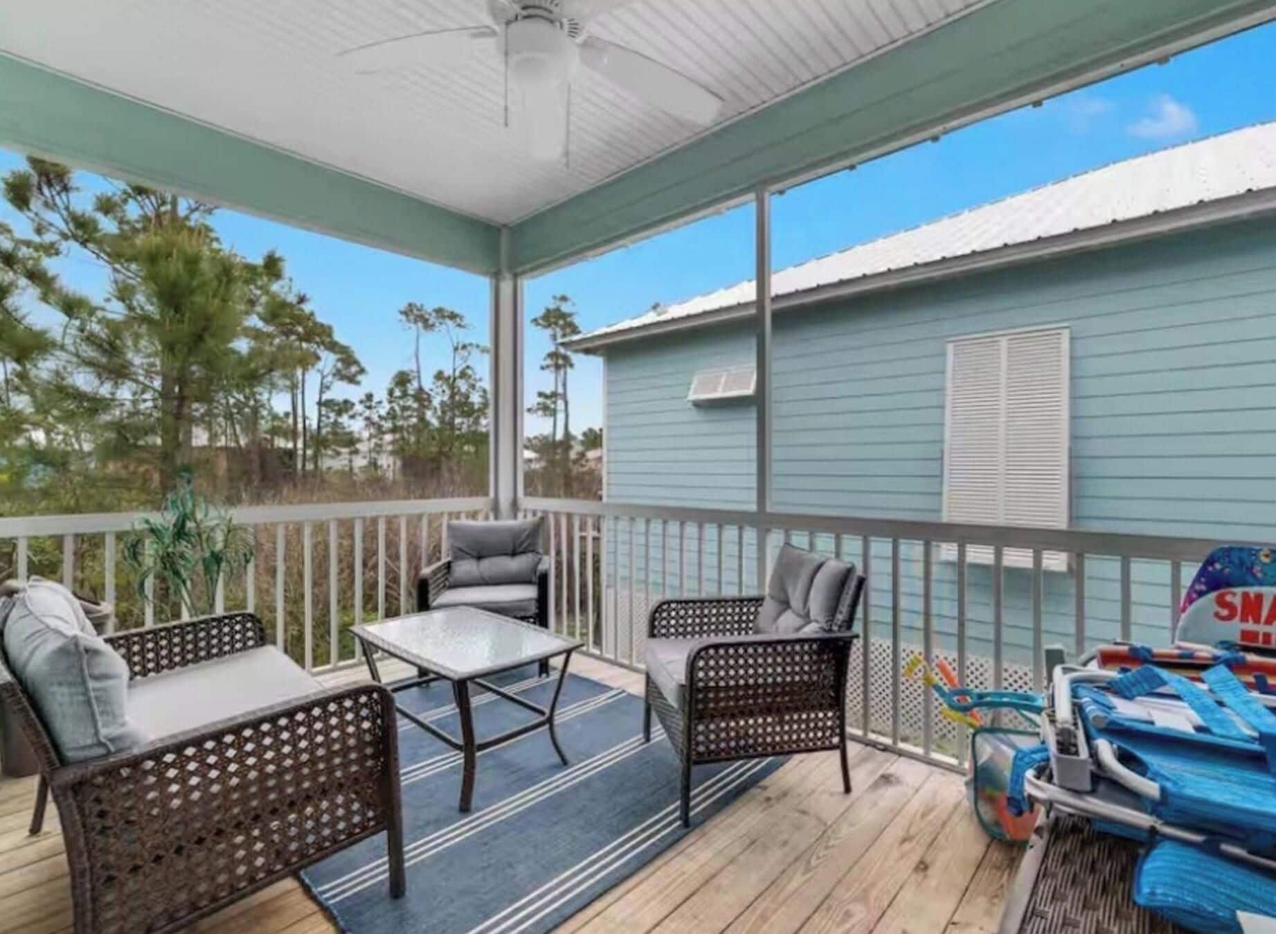 Varanda coberta com móveis de exterior, mesa e vista para uma casa com fachada azul.