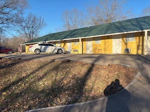 Um edifício amarelo com telhado verde, um estacionamento e um carro.