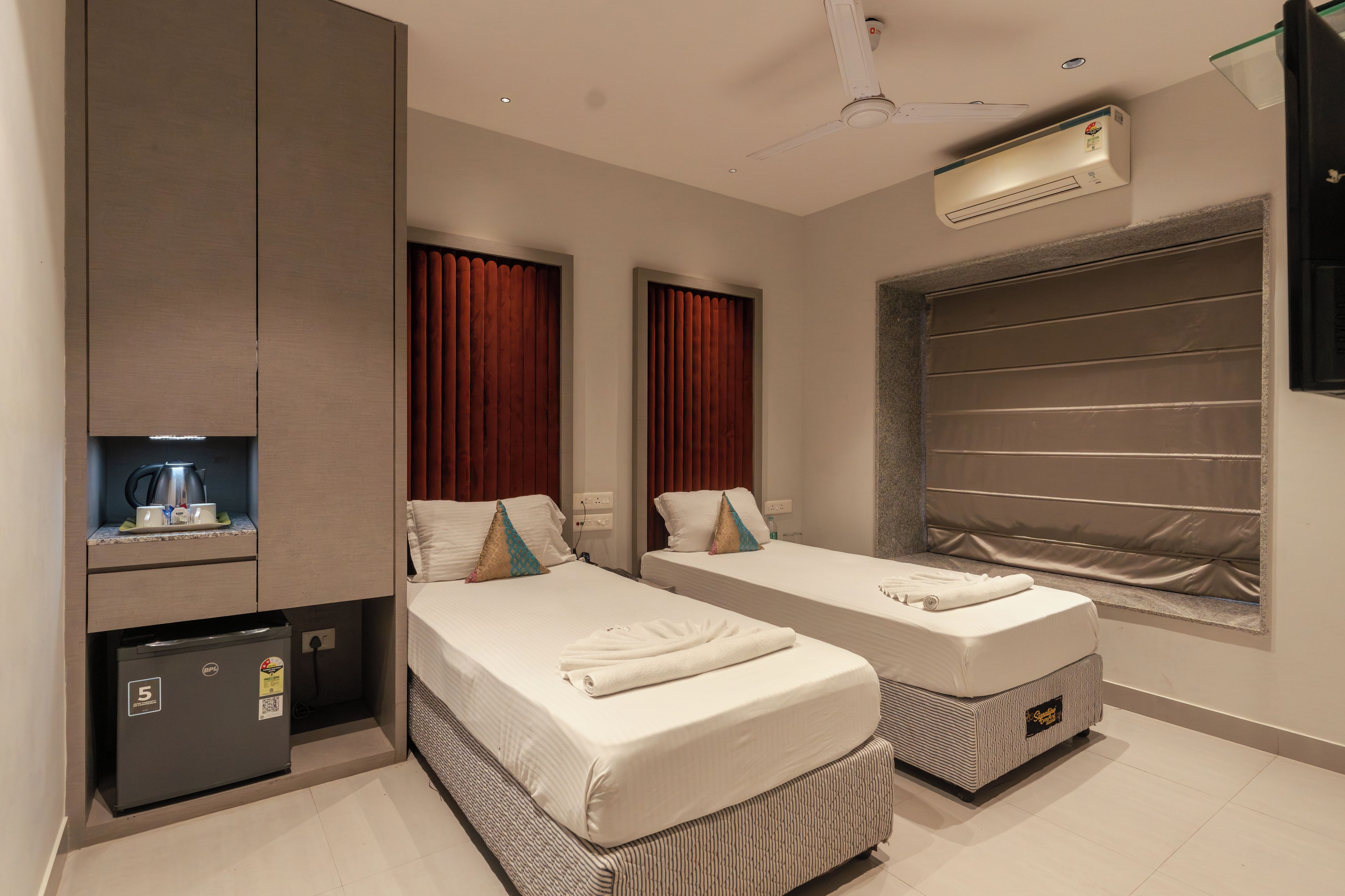 Quarto de hotel com duas camas, cozinha compacta, ventoinha no teto e ar condicionado.