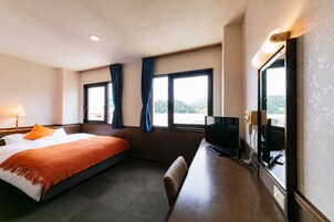 Quarto de hotel com cama, escrivaninha com televisão e janelas com cortinas.