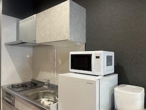 Cozinha compacta com micro-ondas sobre uma geladeira branca, uma pia de aço inoxidável e um fogão a gás.
