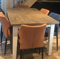 Mesa de jantar com quatro cadeiras, escada ao fundo e área de cozinha.