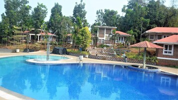 Piscina com deck ao redor, área de estar coberta e edifícios residenciais ao fundo.