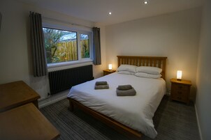 Quarto com uma cama grande, duas mesas de cabeceira com luminárias, uma janela com cortinas e um radiador.