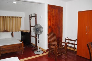 Quarto com cama, ventilador, cadeira de madeira, guarda-roupa e porta.