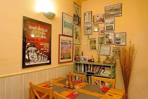 Uma área de refeições com uma mesa de madeira posta para dois, rodeada por estantes repletas de livros.