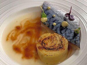 Prato com um pedaço de peixe e um item redondo, possivelmente batata, com molho.