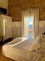 Quarto com cama, guarda-roupa e vista para o mar através de cortinas leves.
