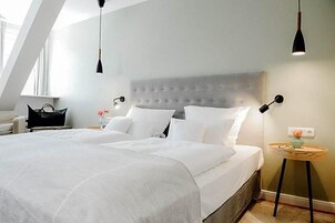 Quarto moderno com cama grande, cabeceira estofada cinza, abajures e pequena mesa lateral de madeira com um vaso.