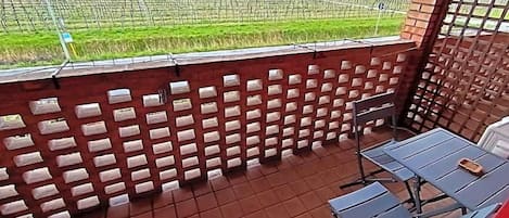 Um terraço com parede de tijolos, uma mesa com cadeiras e vista para um vinhedo.