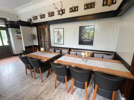 Uma área de refeições com uma mesa de madeira comprida, cadeiras pretas e toalha de mesa branca.