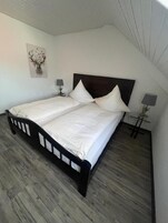 Quarto com uma cama, duas mesas de cabeceira, uma luminária na parede e um quadro.