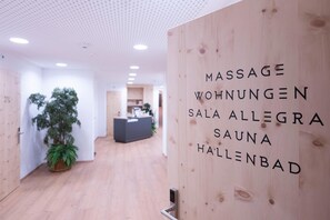 Área de recepção com parede de madeira exibindo informações sobre um espaço de massagem e sauna.