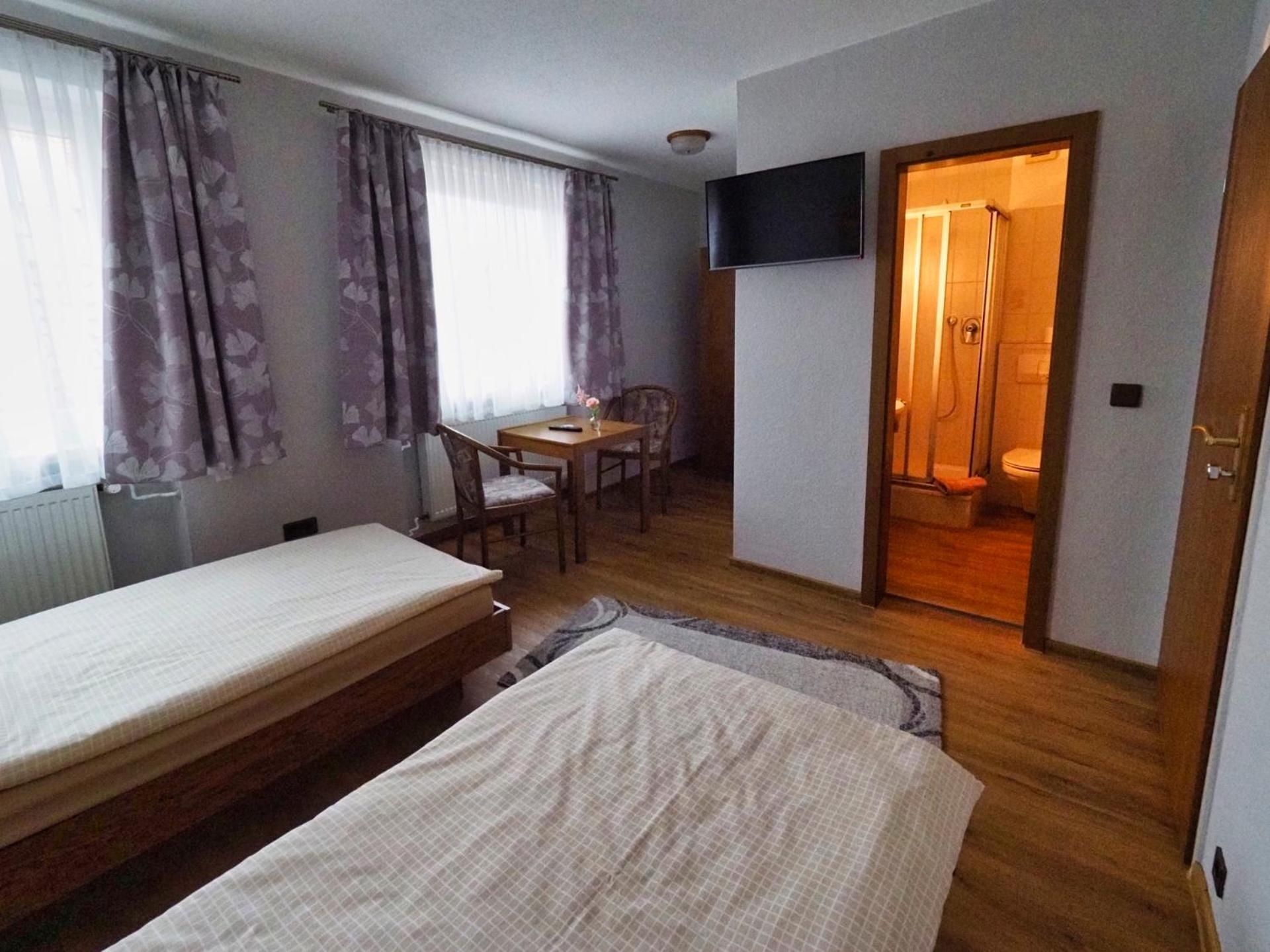 Quarto com duas camas, uma escrivaninha com cadeira, televisão na parede e chuveiro.